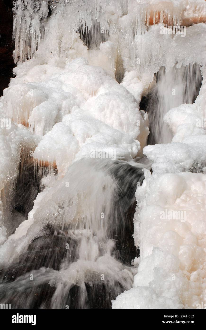 On a freezing cold winter day, the cascade of a water fall flows under ...