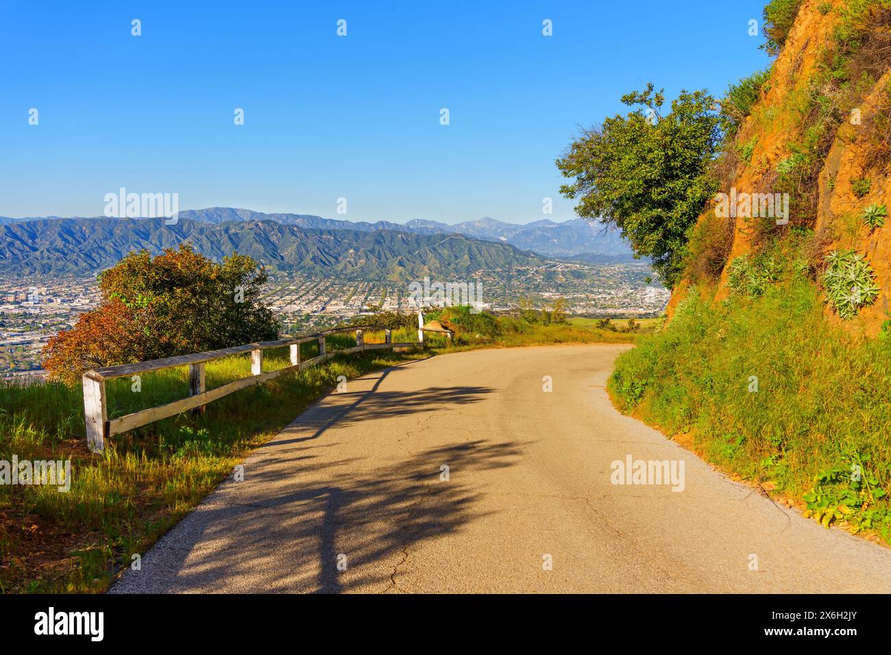 Asphalt trail winds beyond the hill, bordered by a rustic wooden ...