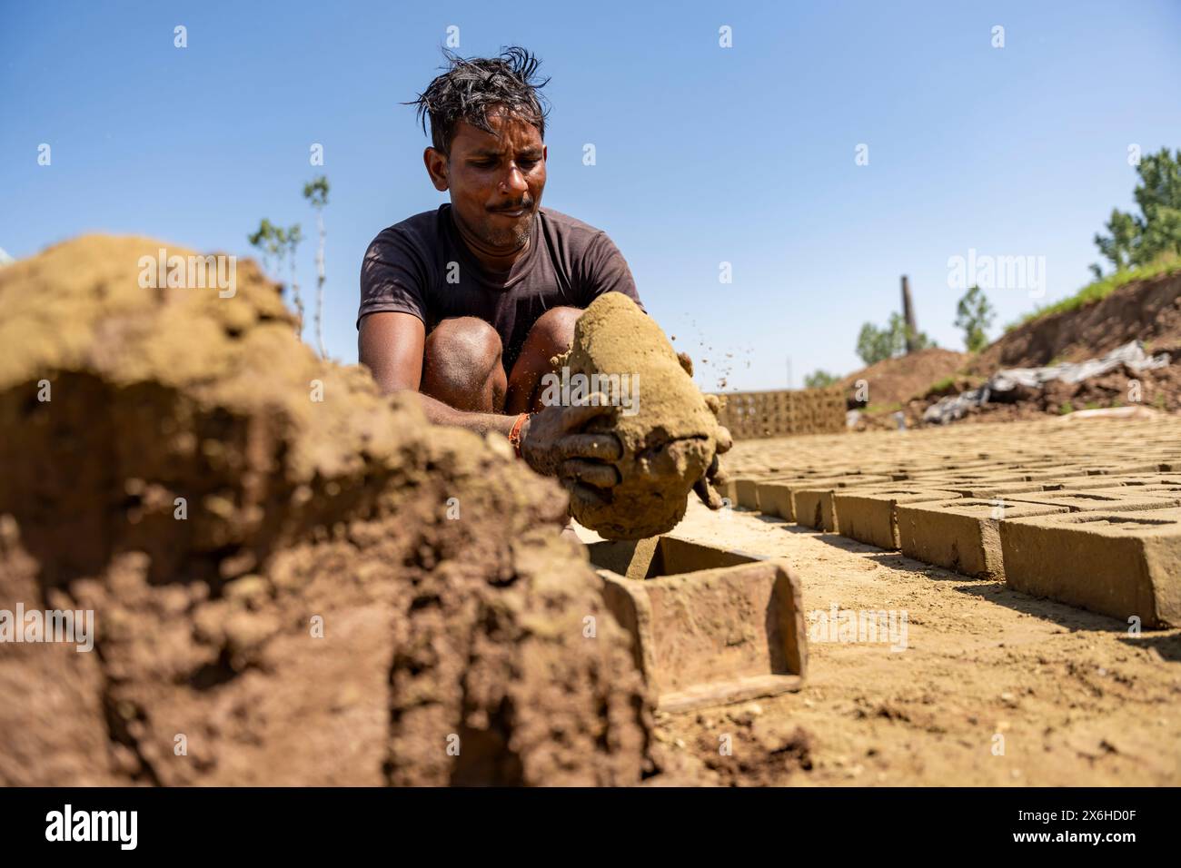 A non-local labourer uses mud to create bricks using a mould at a brick ...