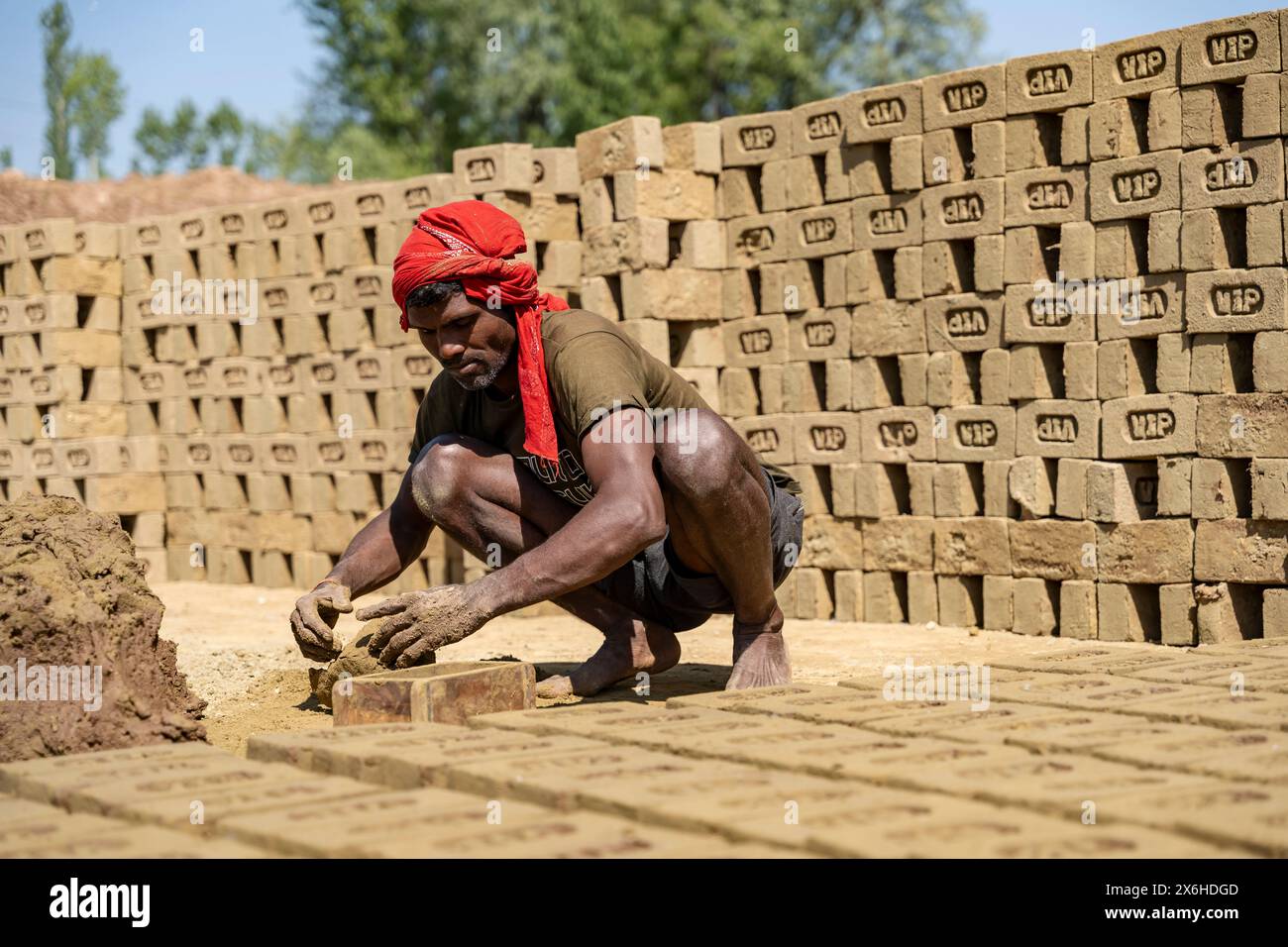 A non-local labourer uses mud to create bricks using a mould at a brick ...