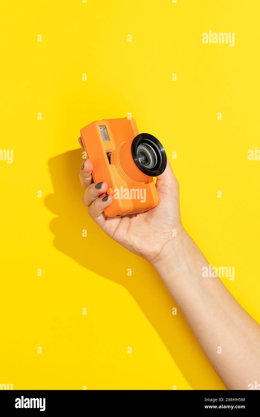 Hand holding orange camera on yellow background Stock Photo - Alamy