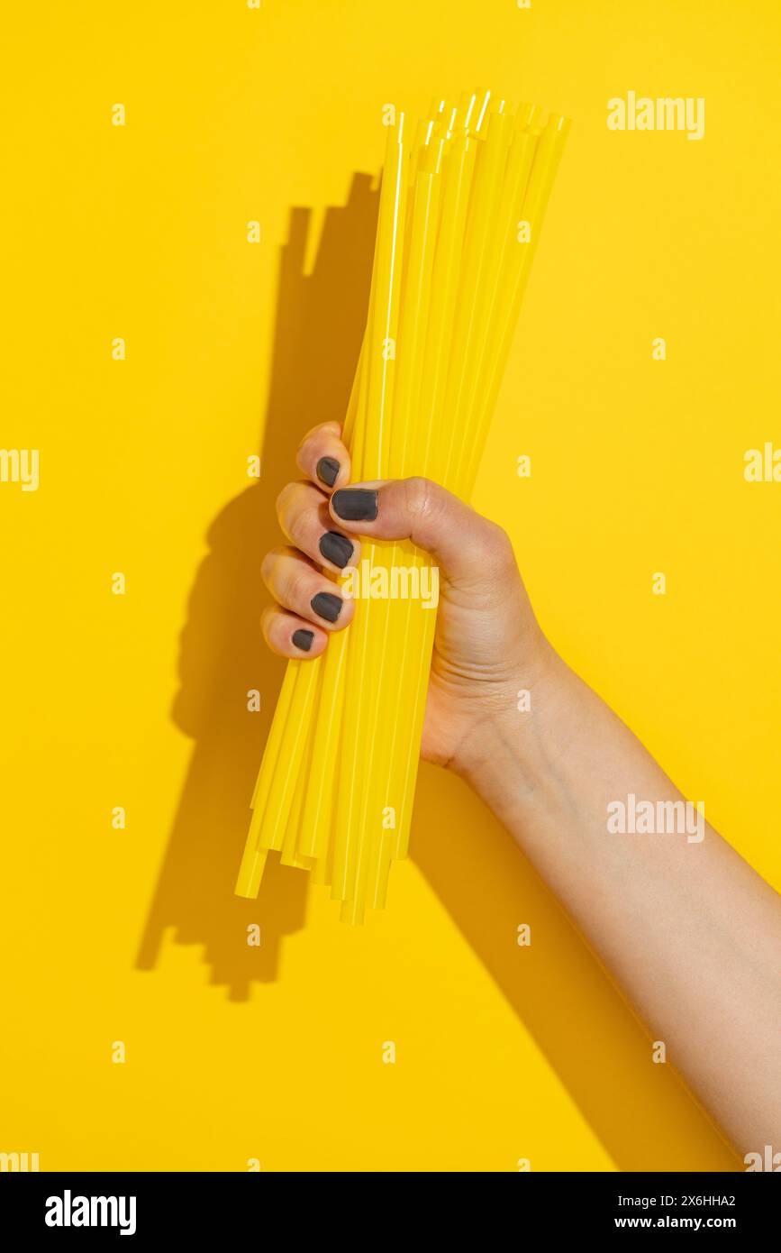 Hand holding bunch of plastic drinking straw on yellow background Stock ...