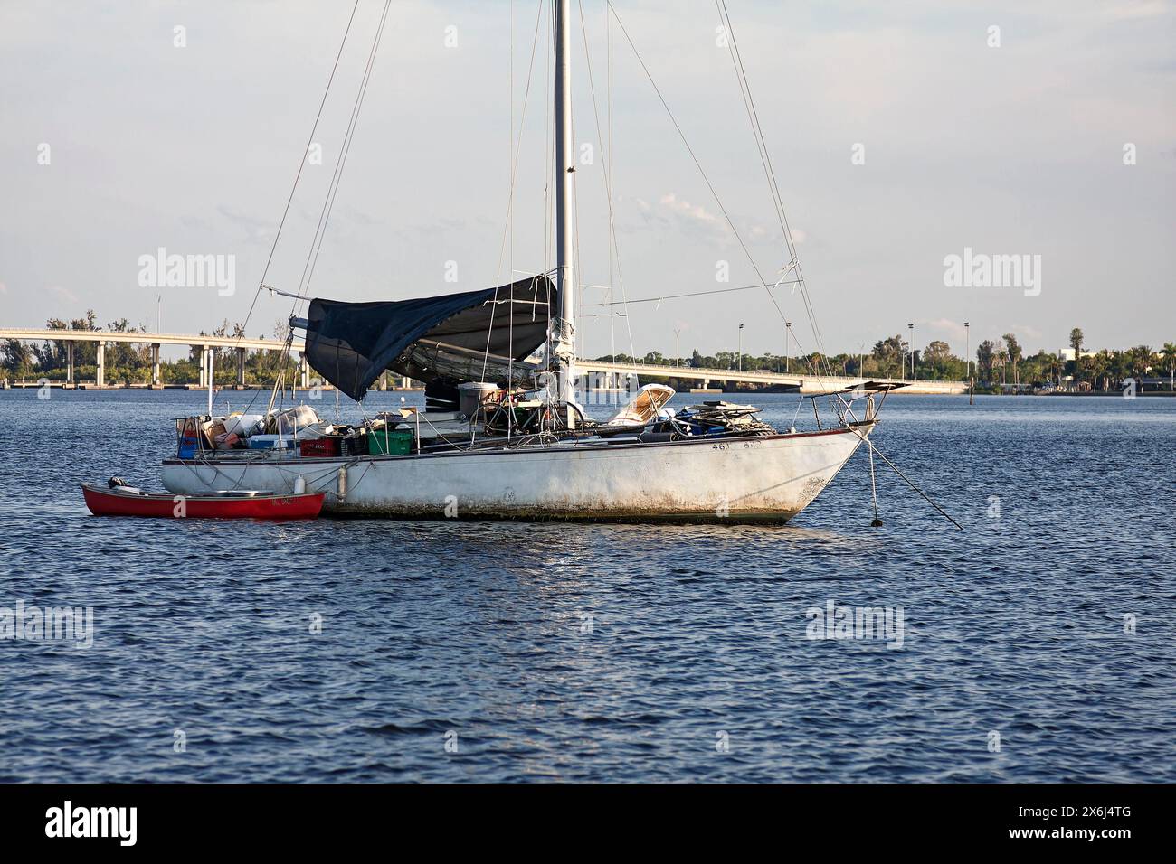 old sailboat, anchored, deck and cockpit filled with things, canoe tied ...