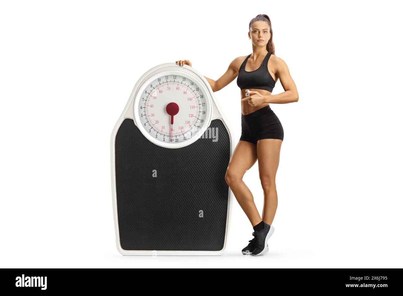 Fit female athlete pointing at a big weight scale isolated on white ...