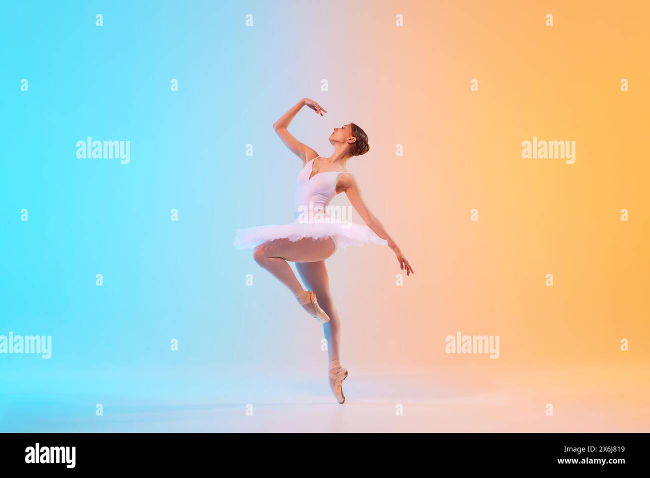 Graceful classic ballerina in white tutu on pointe dancing in motion in neon light against blue ...