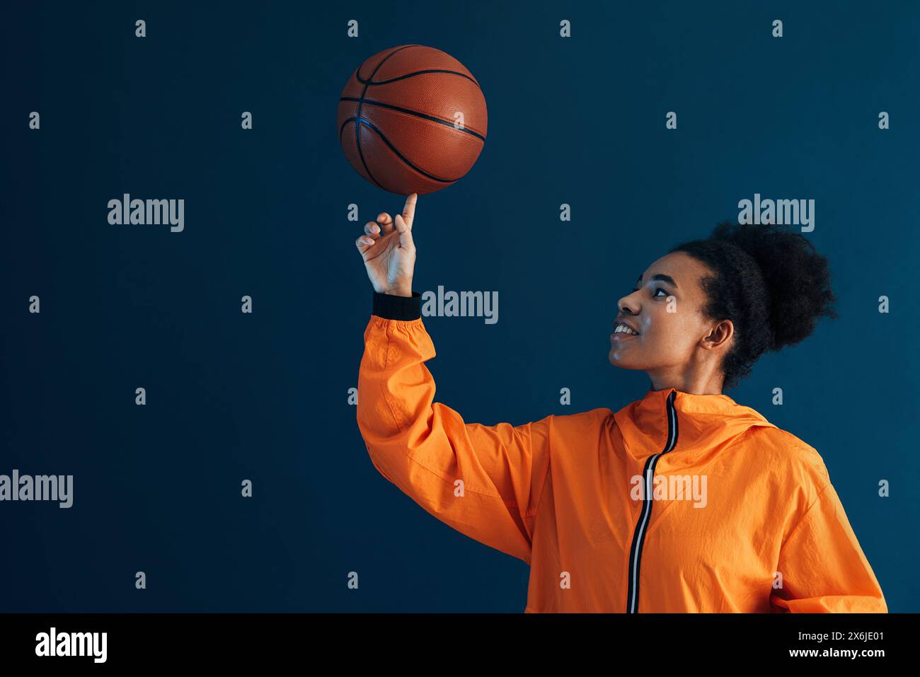 Professional Female Basketball Player Spins A Basketball On Finger Over The Blue Backdrop Young
