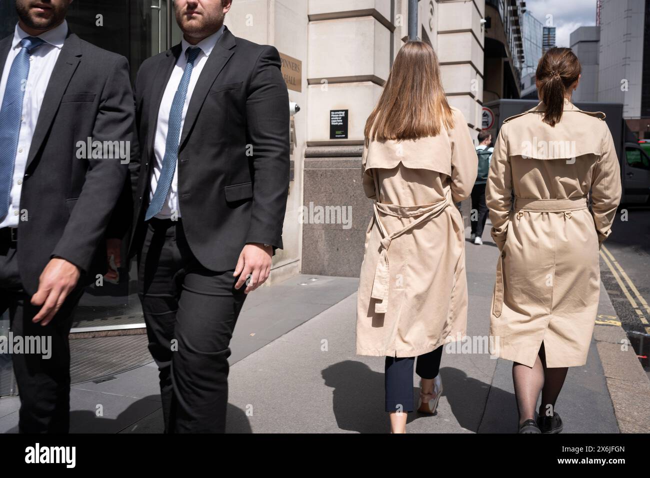 Seen from the rear, two women wear matching macintosh-style coats walk ...