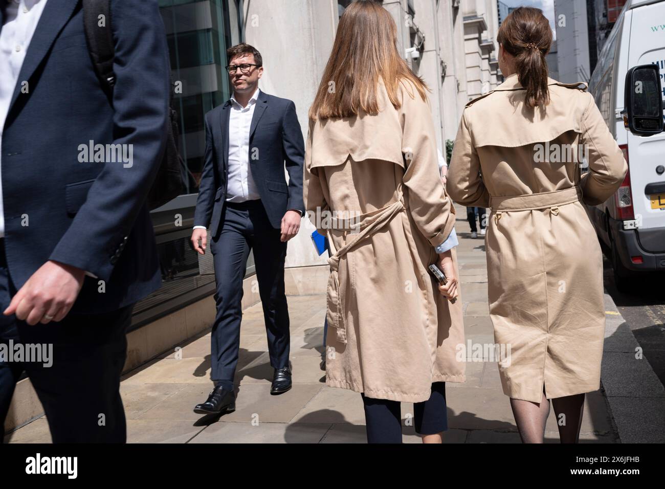 Seen from the rear, two women wear matching macintosh-style coats walk ...