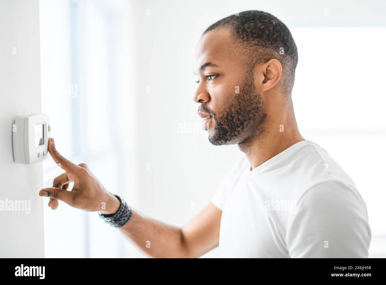 man choosing temperature on thermostat. Young focused guy pushing ...