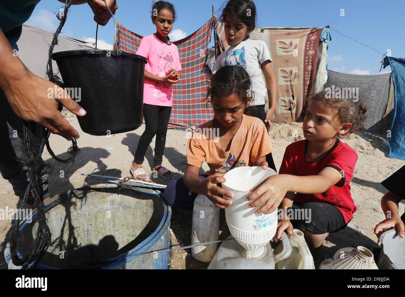 Displaced Palestinians wait to get water from a traditional water well ...