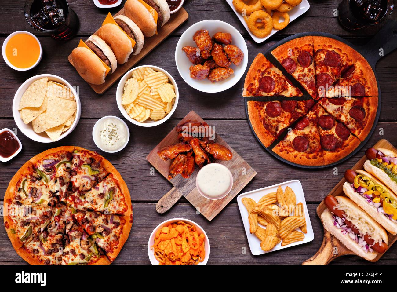 Junk food table scene. Pizza, hamburgers, hot dogs, chicken wings and ...