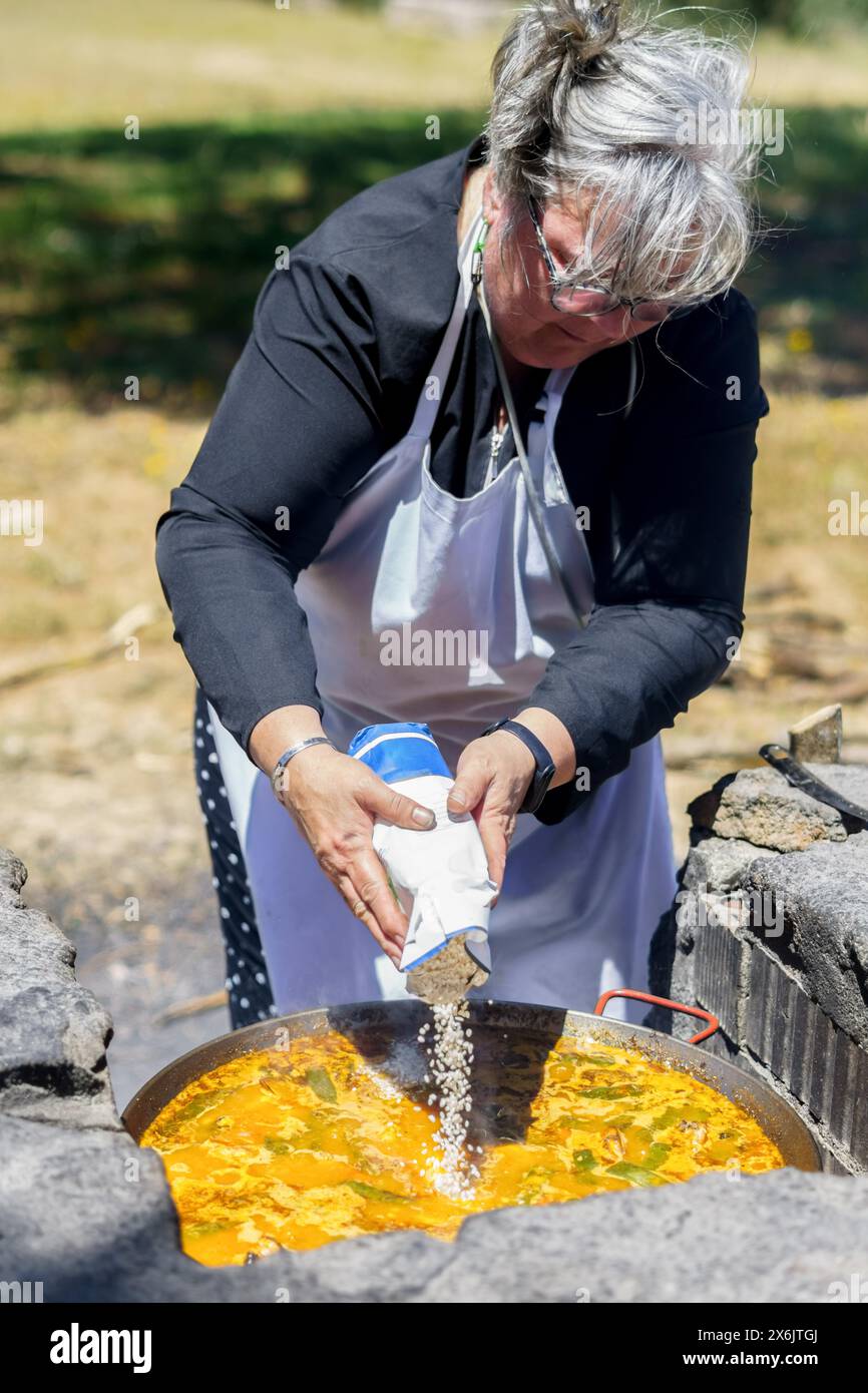 Woman cook in white apron pouring rice into a typical Spanish paella ...