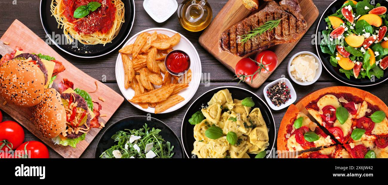 Table scene with a selection of delicious foods. Top view over a dark ...