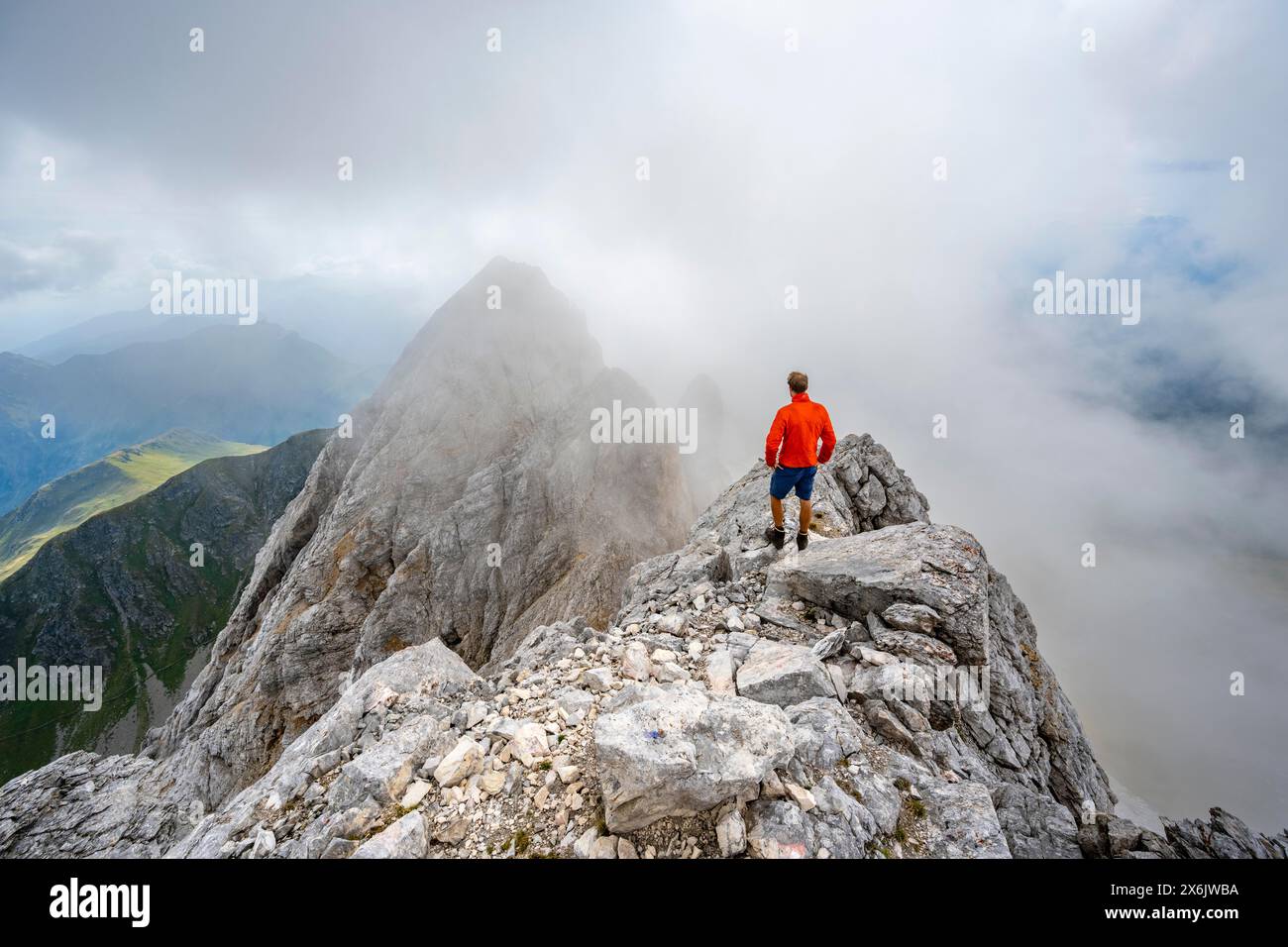 Mountaineer on a rocky narrow summit ridge, cloudy mountain peak ...