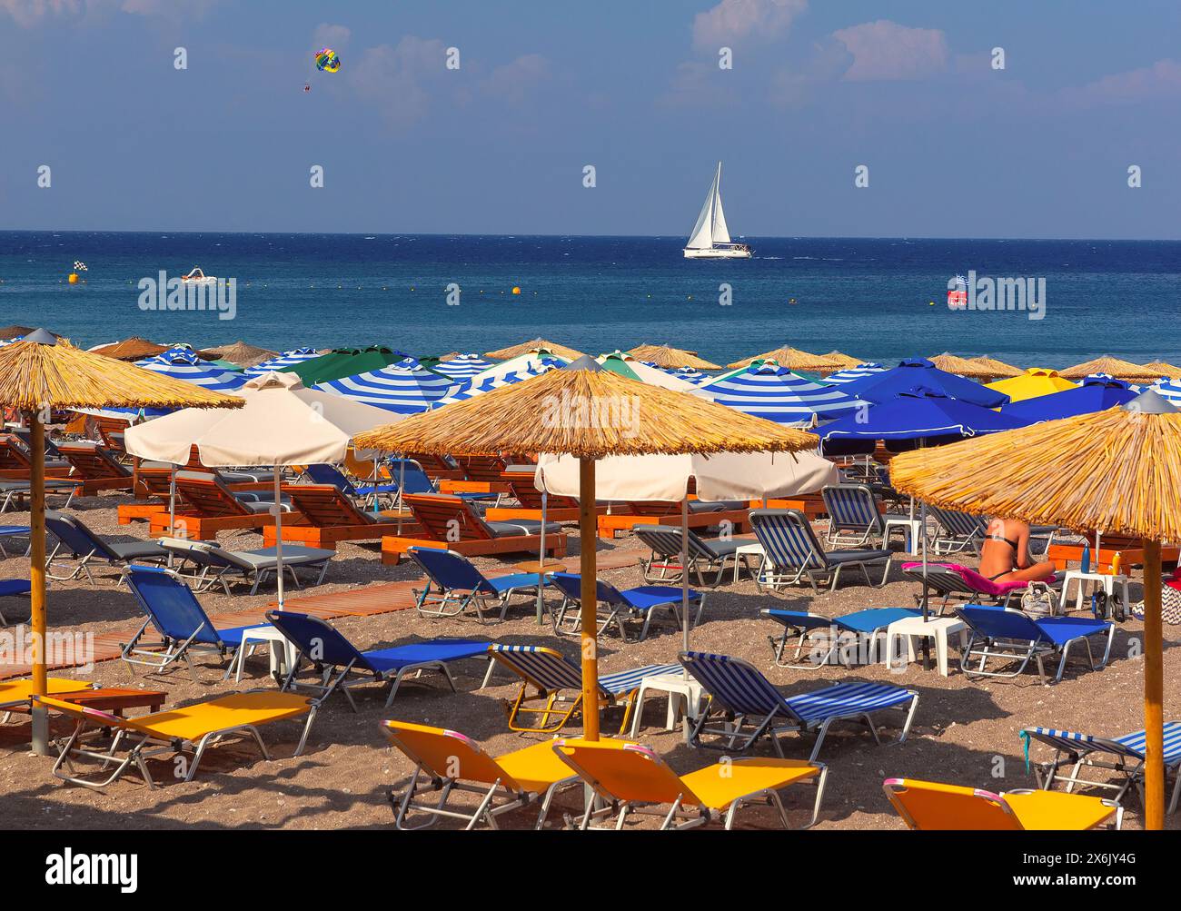 Colorful beach scene in Rhodes, Greece, with loungers and sailing boat ...