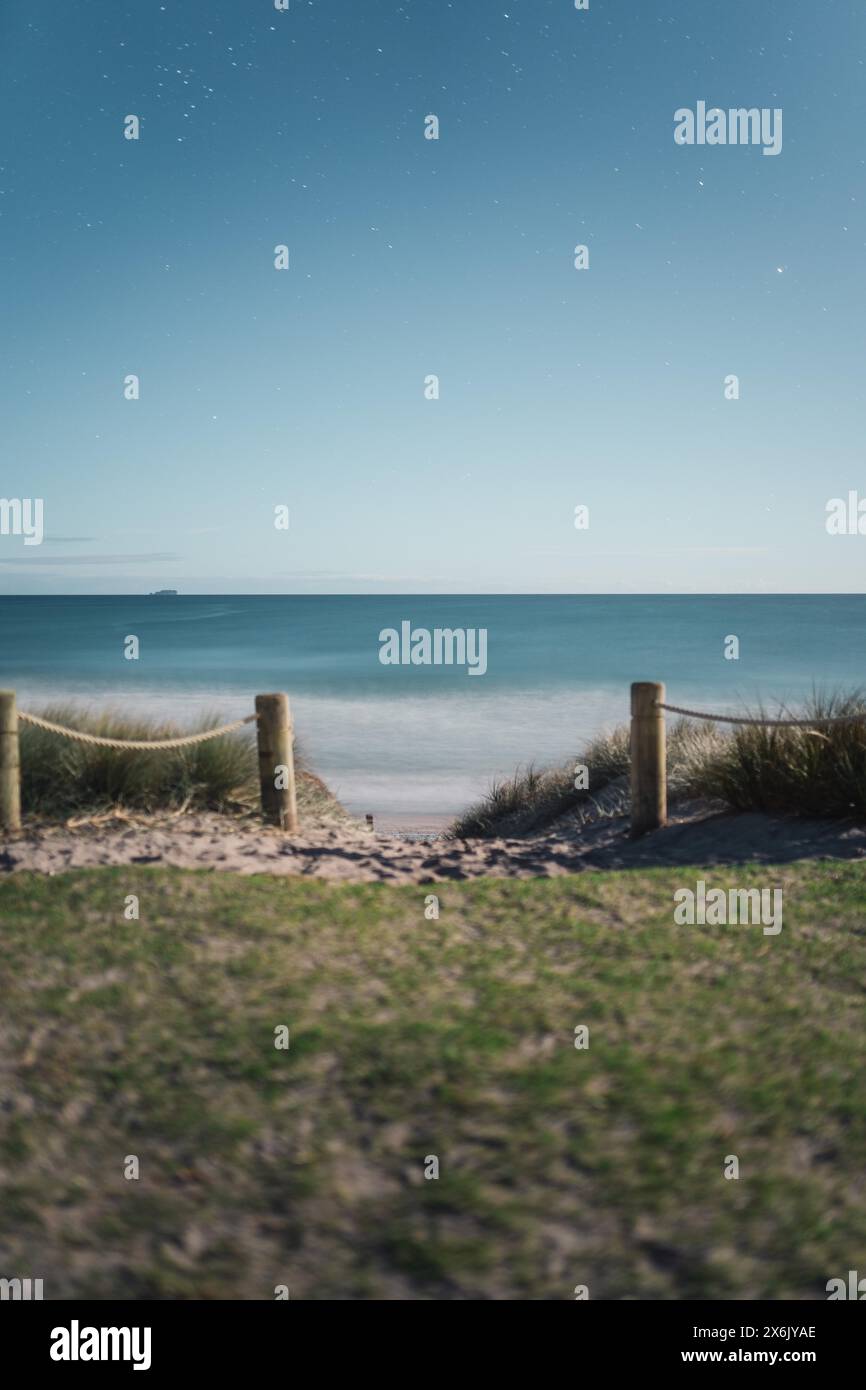 Starry night sky over a quiet beach and sea, demarcated by wooden posts ...