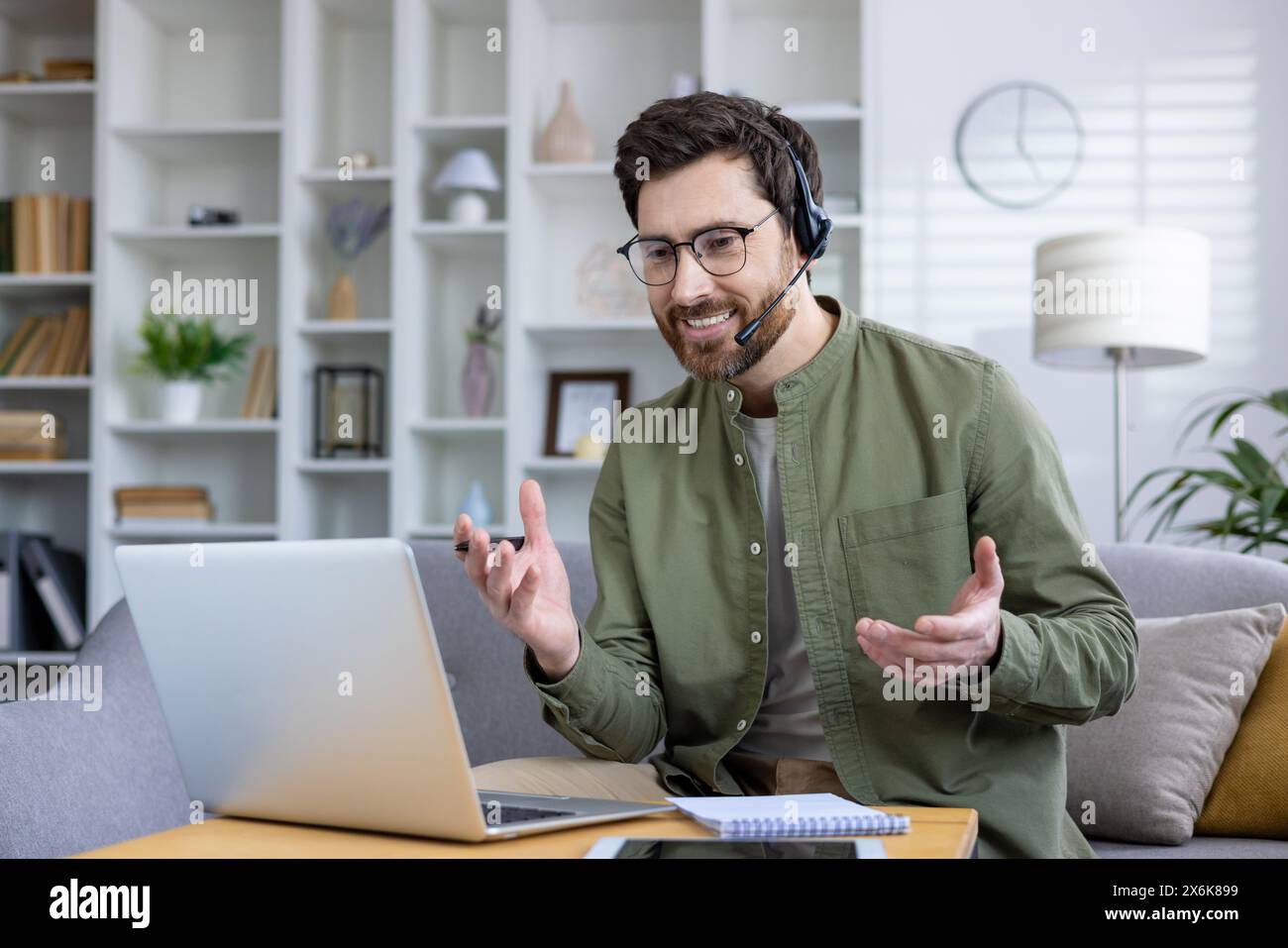 Man in casual attire using a laptop and headset for a work meeting in a ...