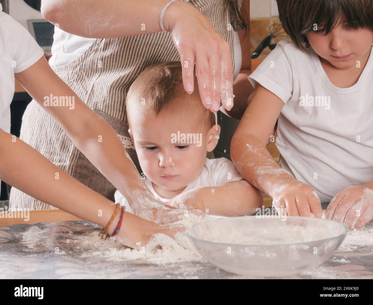 A woman is helping a baby make a cake. The baby is covered in flour and ...