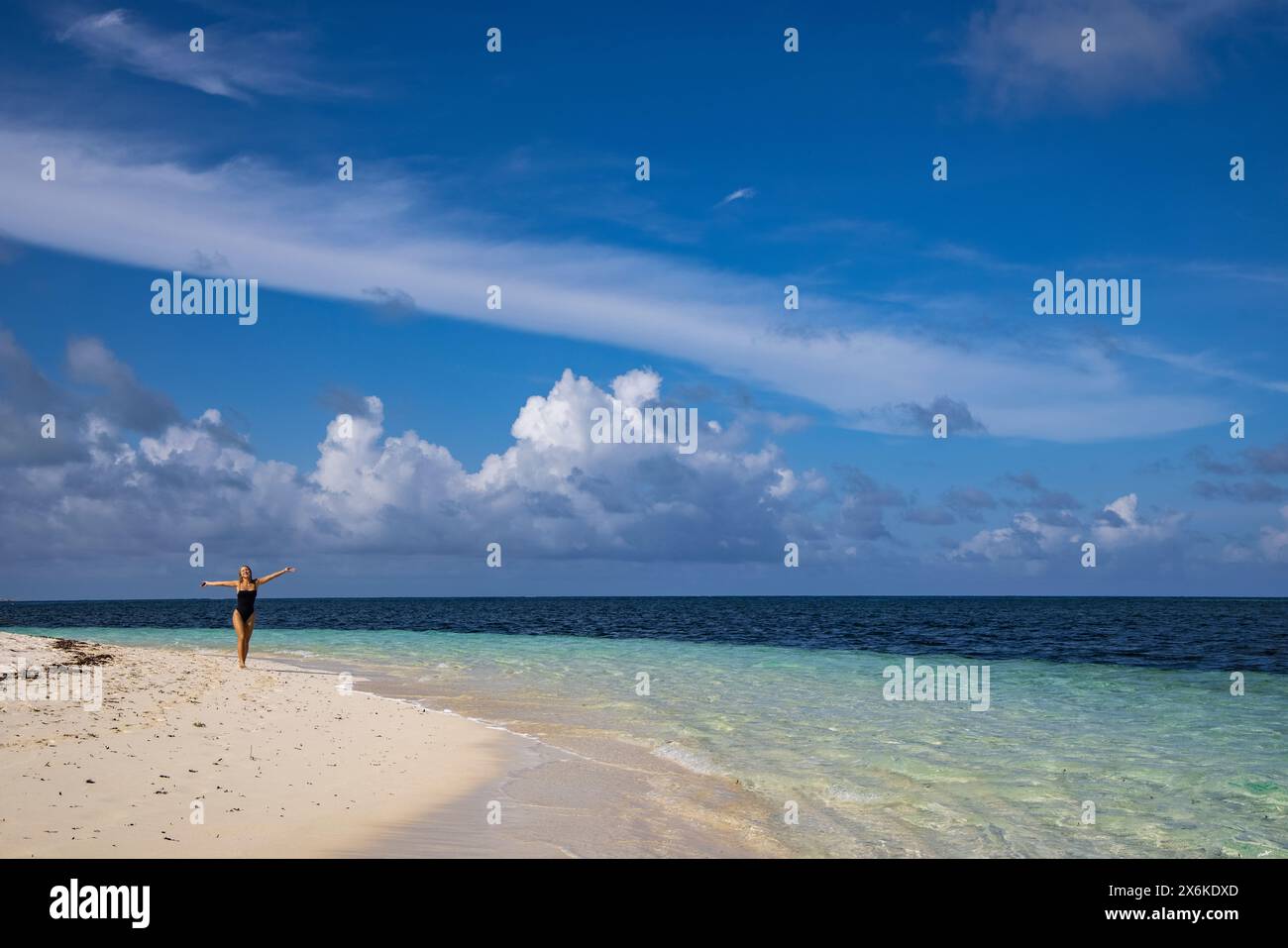 Woman spreads her arms while strolling along beach of Bijoutier Island ...