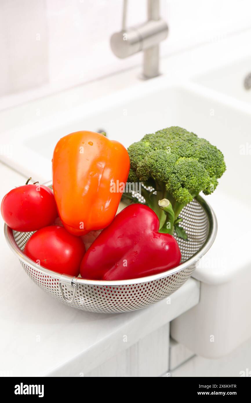 Fresh clean vegetables in colander on countertop near sink Stock Photo ...