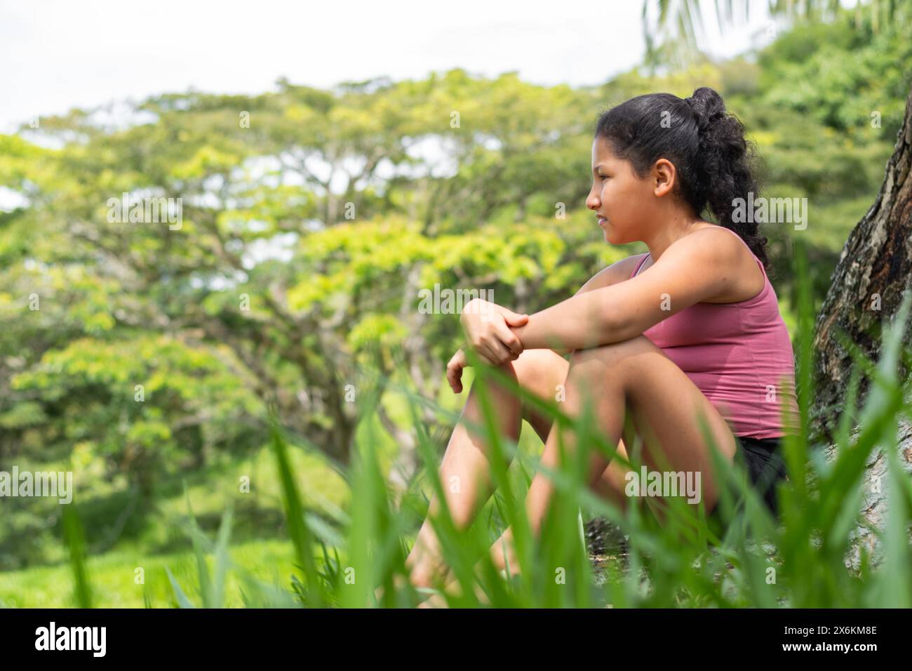 latina brunette girl sitting next to a tree looking towards the horizon ...
