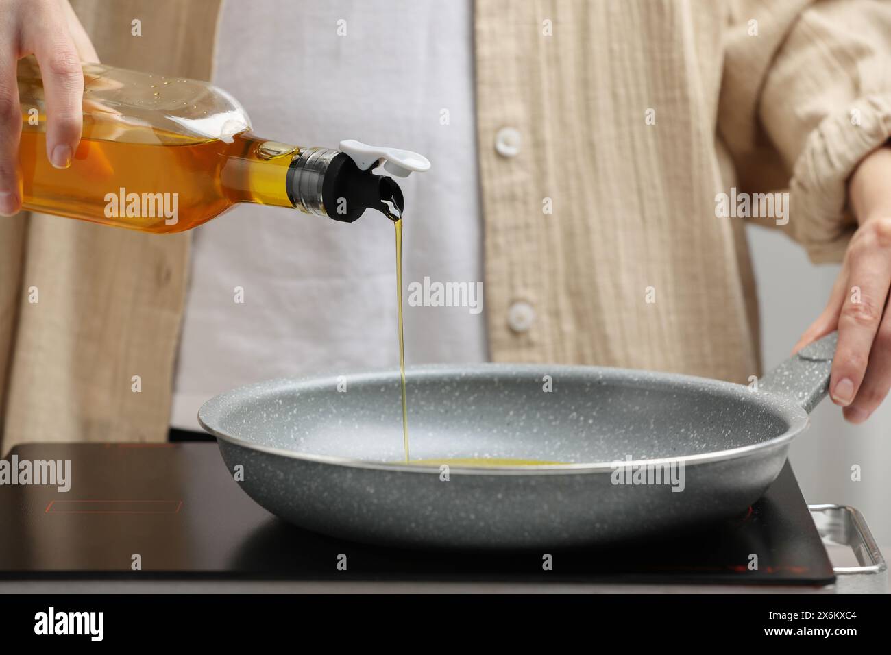 Vegetable fats. Woman pouring cooking oil into frying pan on stove ...
