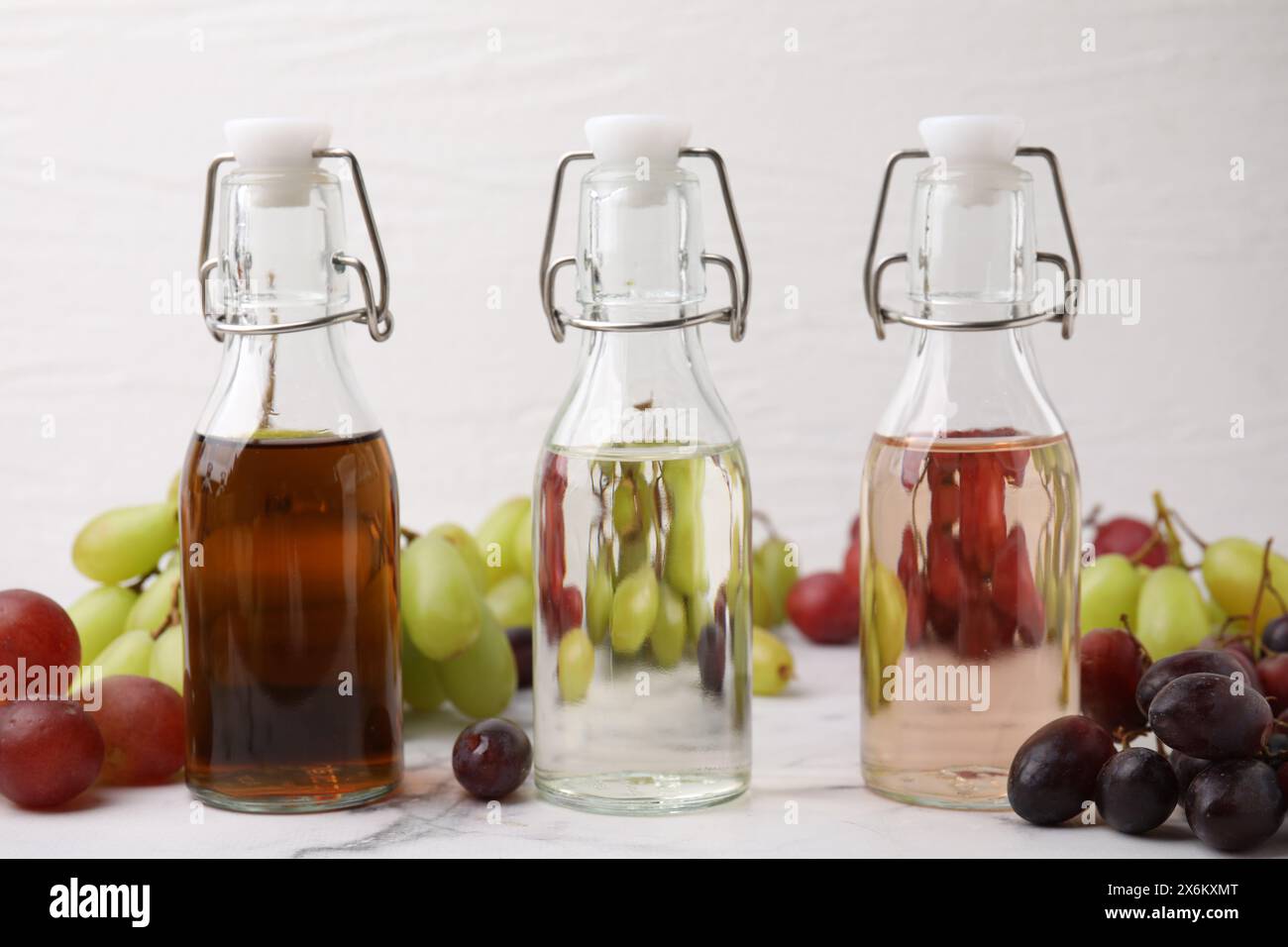 Different types of vinegar in bottles and grapes on light marble table ...