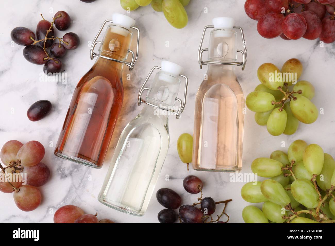 Different types of vinegar in bottles and grapes on light marble table ...