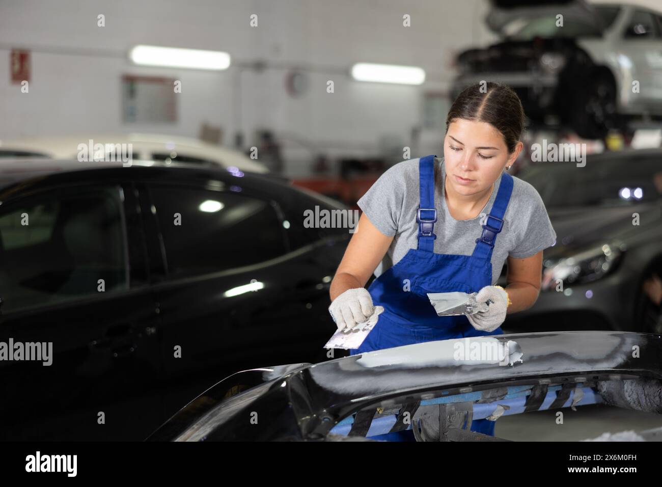 Young woman mechanic repairing car with putty and spatula Stock Photo ...