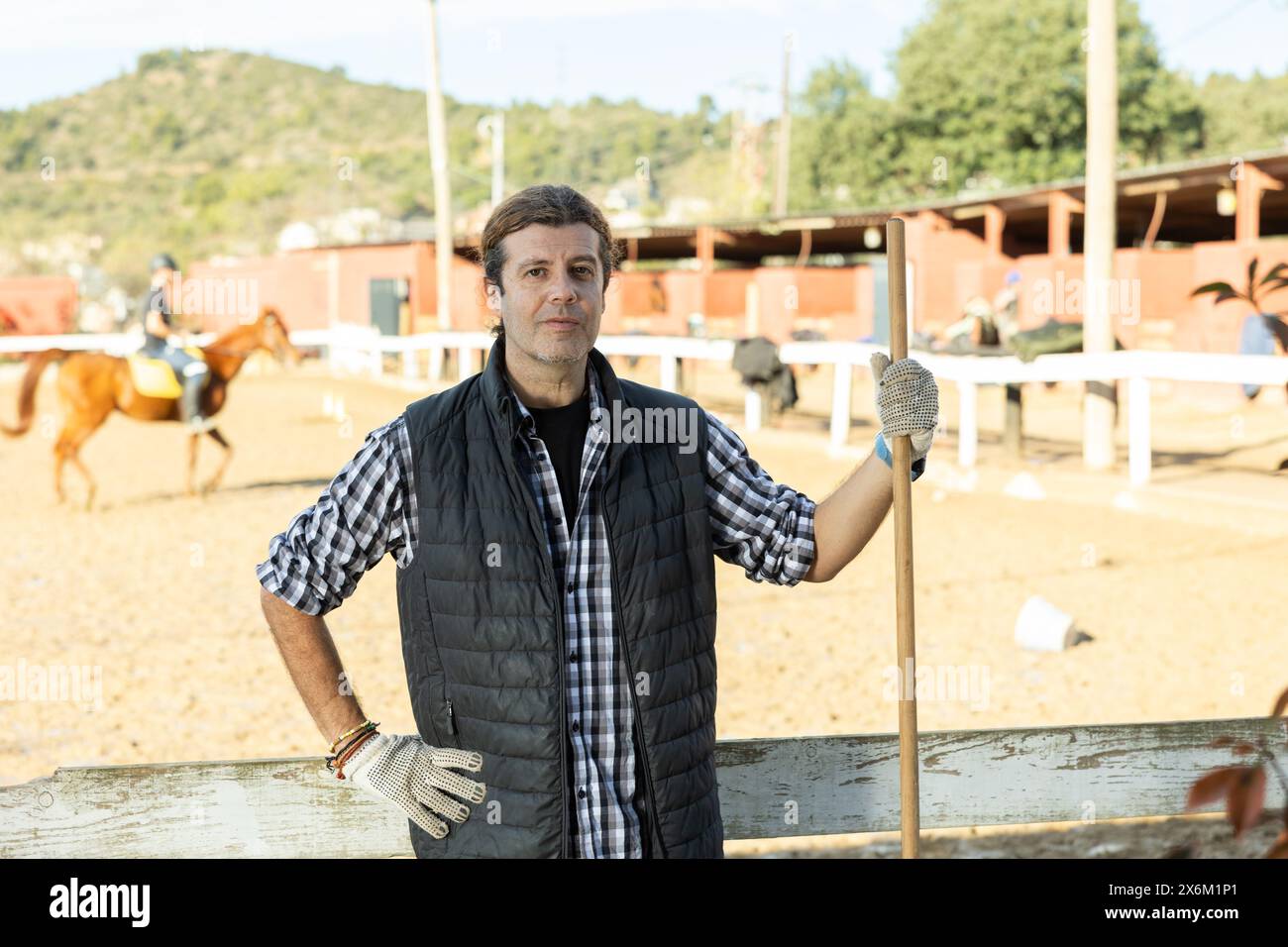 Skilled adult man stables worker in plaid shirt looking at camera while ...