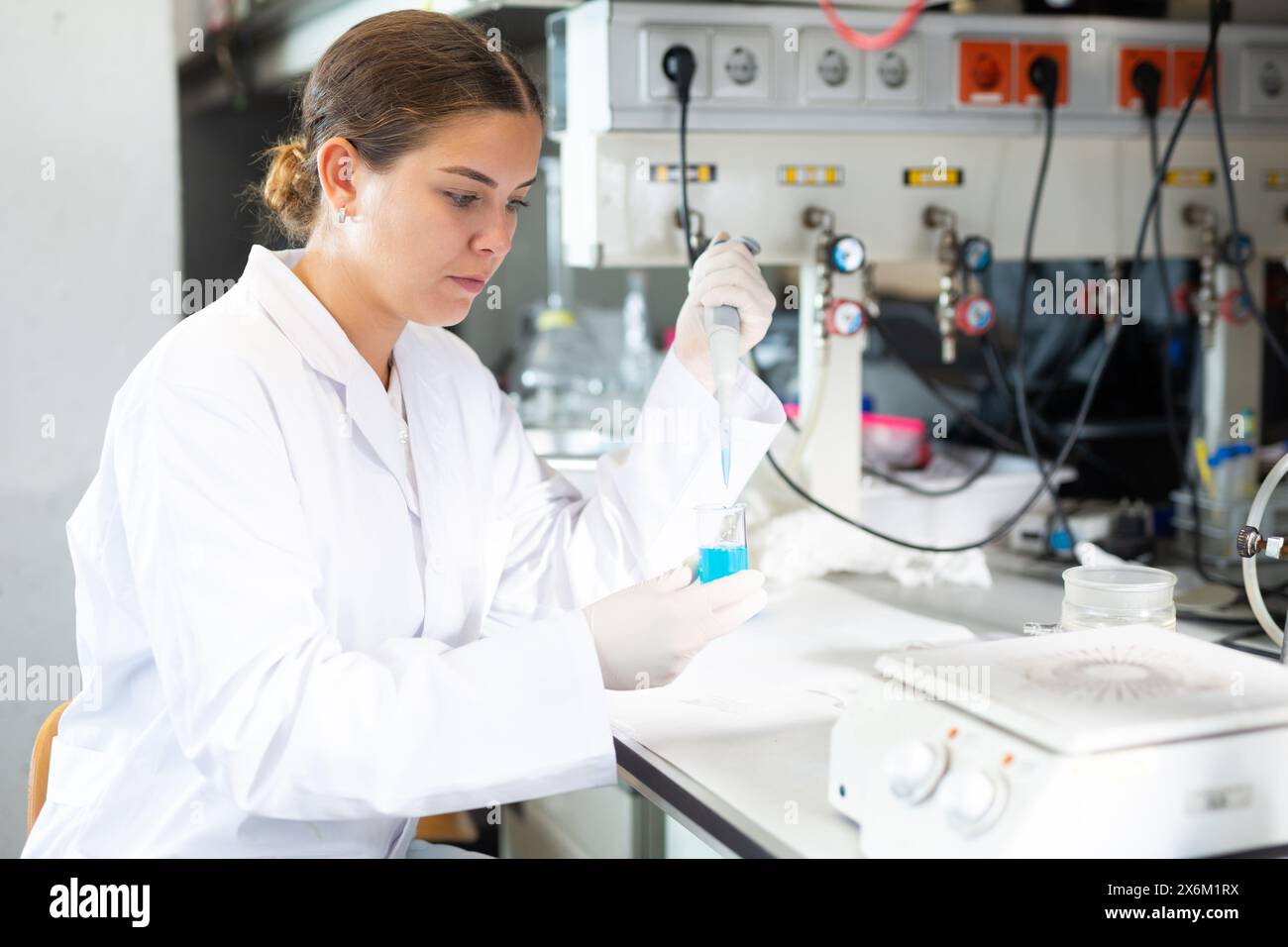 Smart young woman biologist in white coat using mechanical lab pipette ...