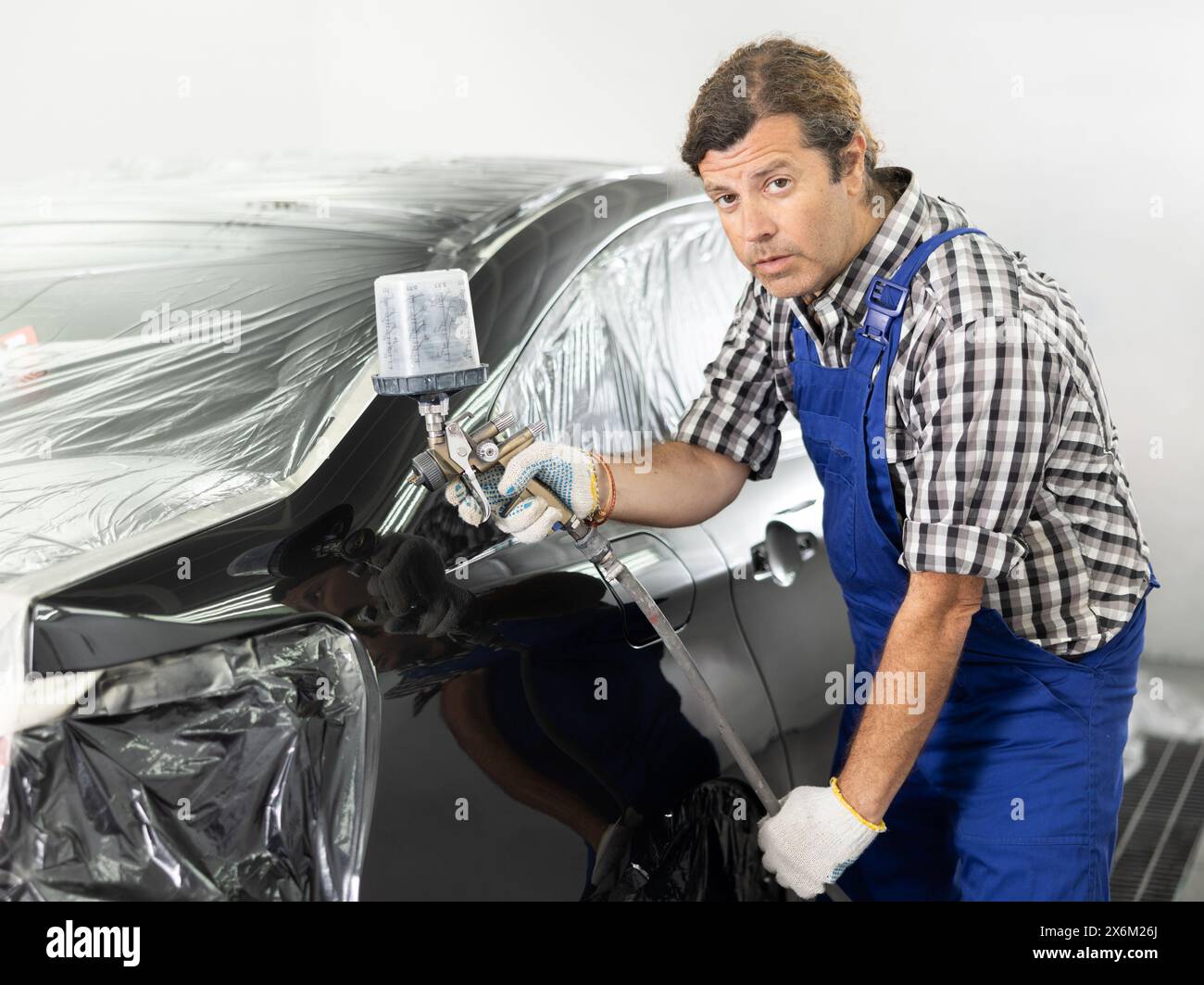 Middle aged man using spray gun to paint car in workshop Stock Photo ...