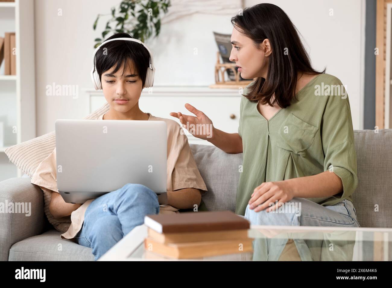 Teenage boy in headphones with laptop ignoring his mother at home ...