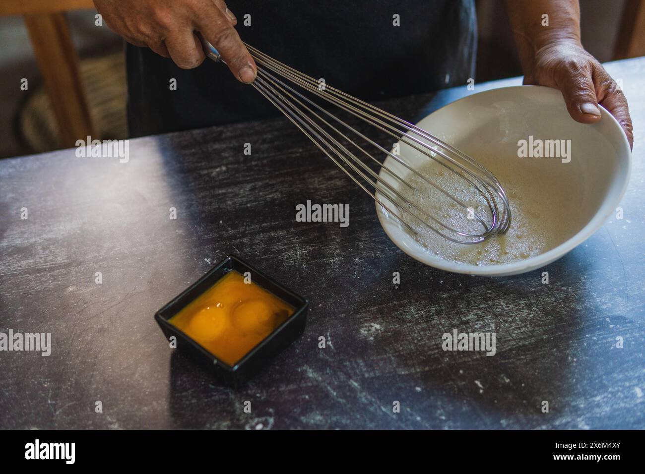 Baker's hands beating eggs with a hand mixer on a white plate ...