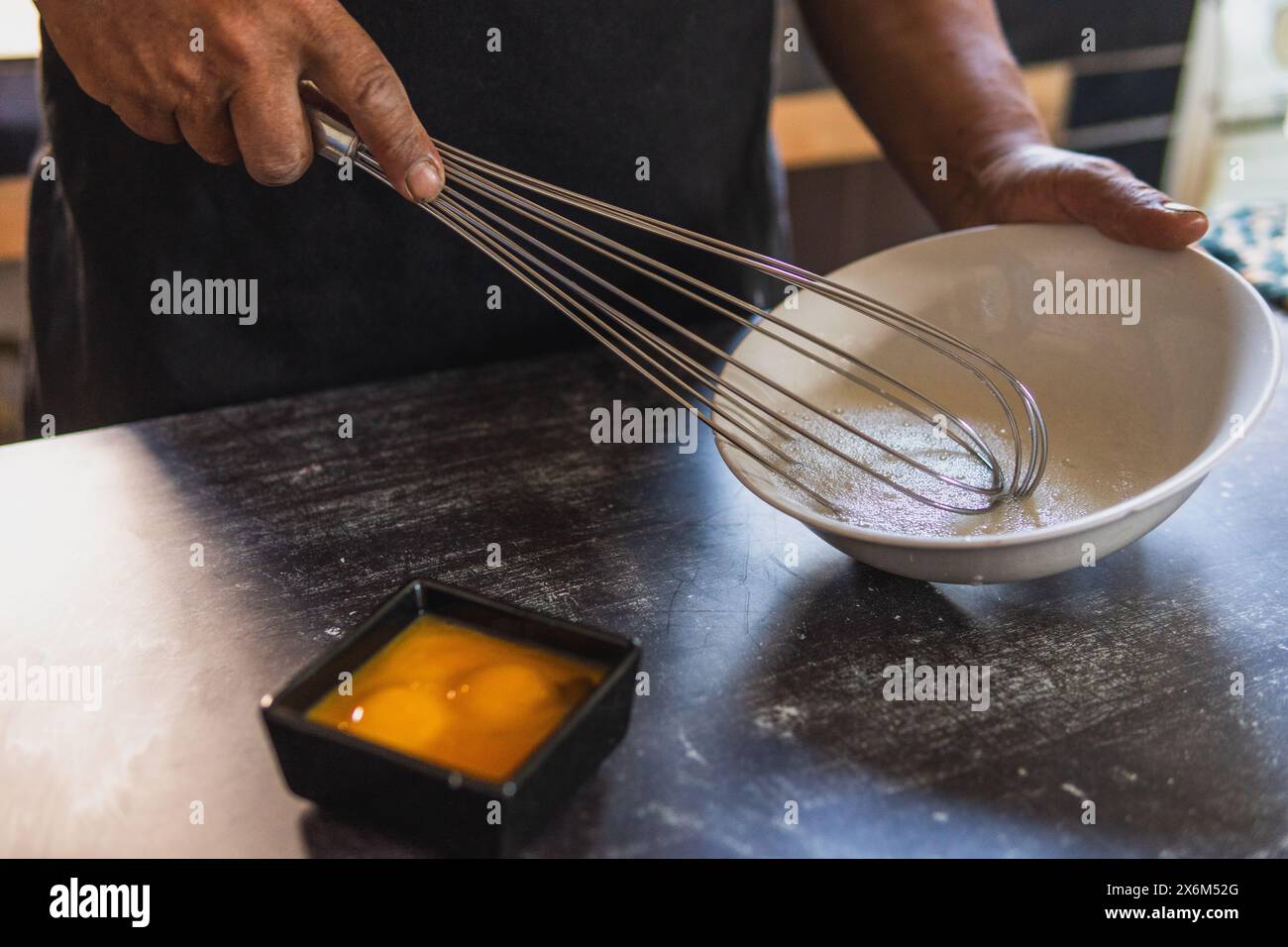 Baker's hands beating eggs with a hand mixer on a white plate ...
