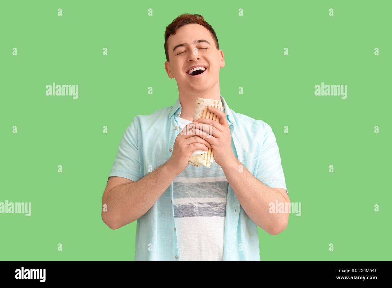 Young happy man eating doner kebab on green background Stock Photo - Alamy