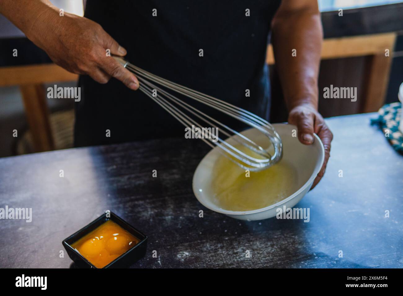 Baker's hands beating eggs with a hand mixer on a white plate, separating the yolks from the ...