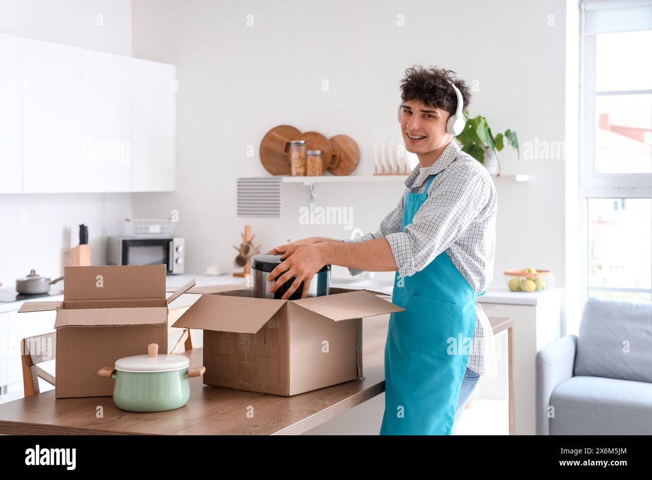 Male janitor with headphones unpacking moving boxes in kitchen Stock ...