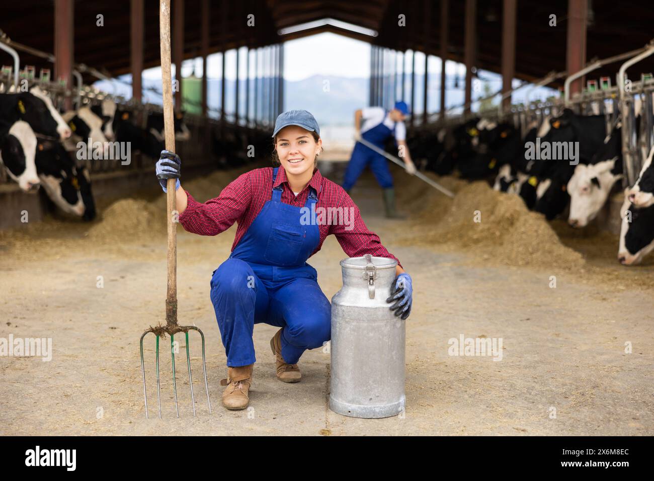 Farmer woman holds rake and can at cow farm Stock Photo - Alamy