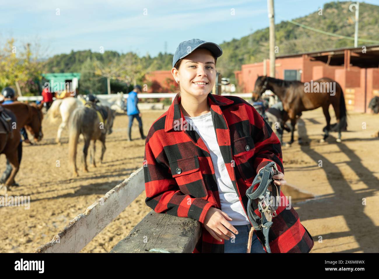 Portrait of positive young female stable worker holding horse halter or ...