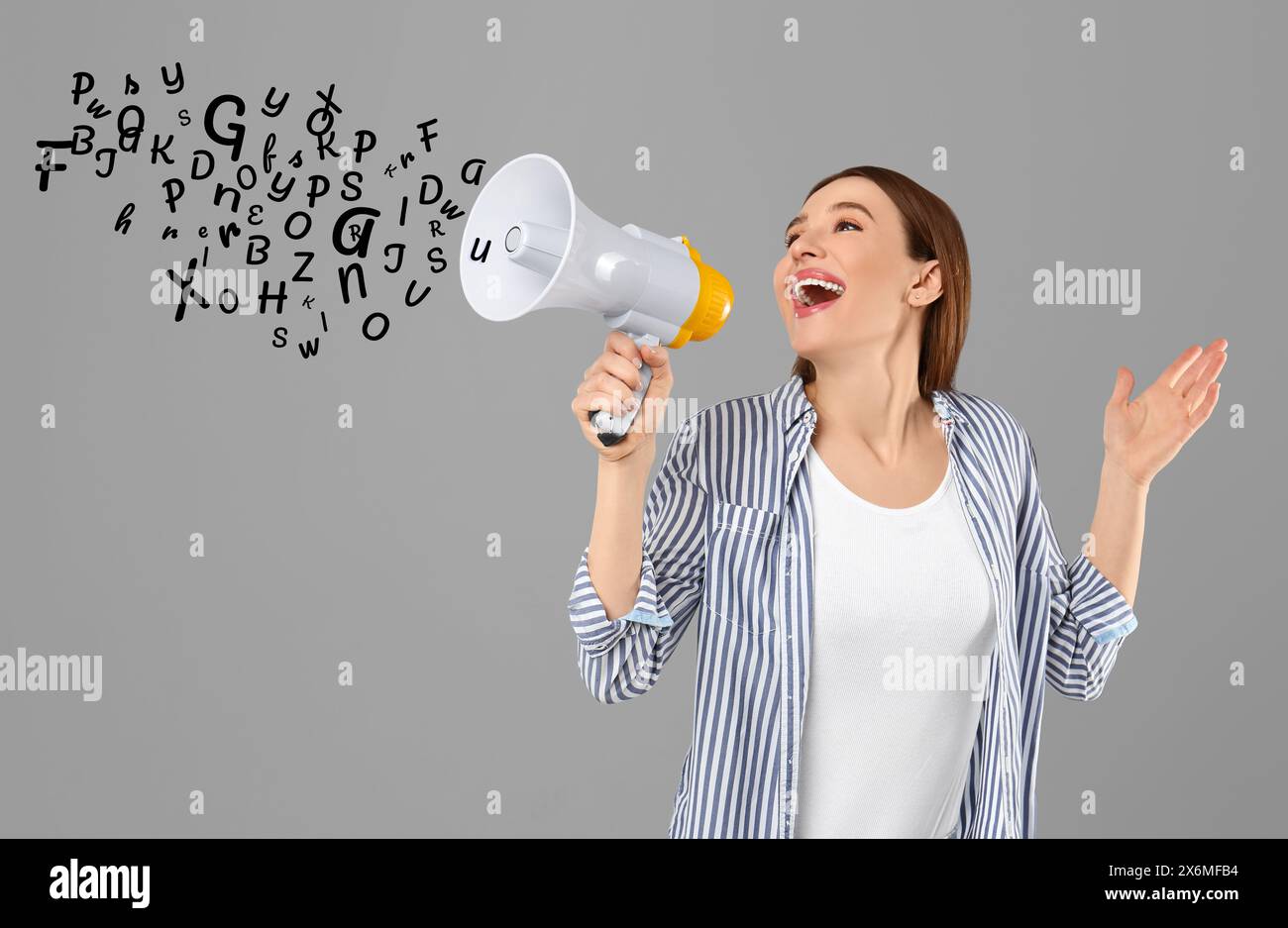 Woman using megaphone on grey background. Letters flying out of device ...