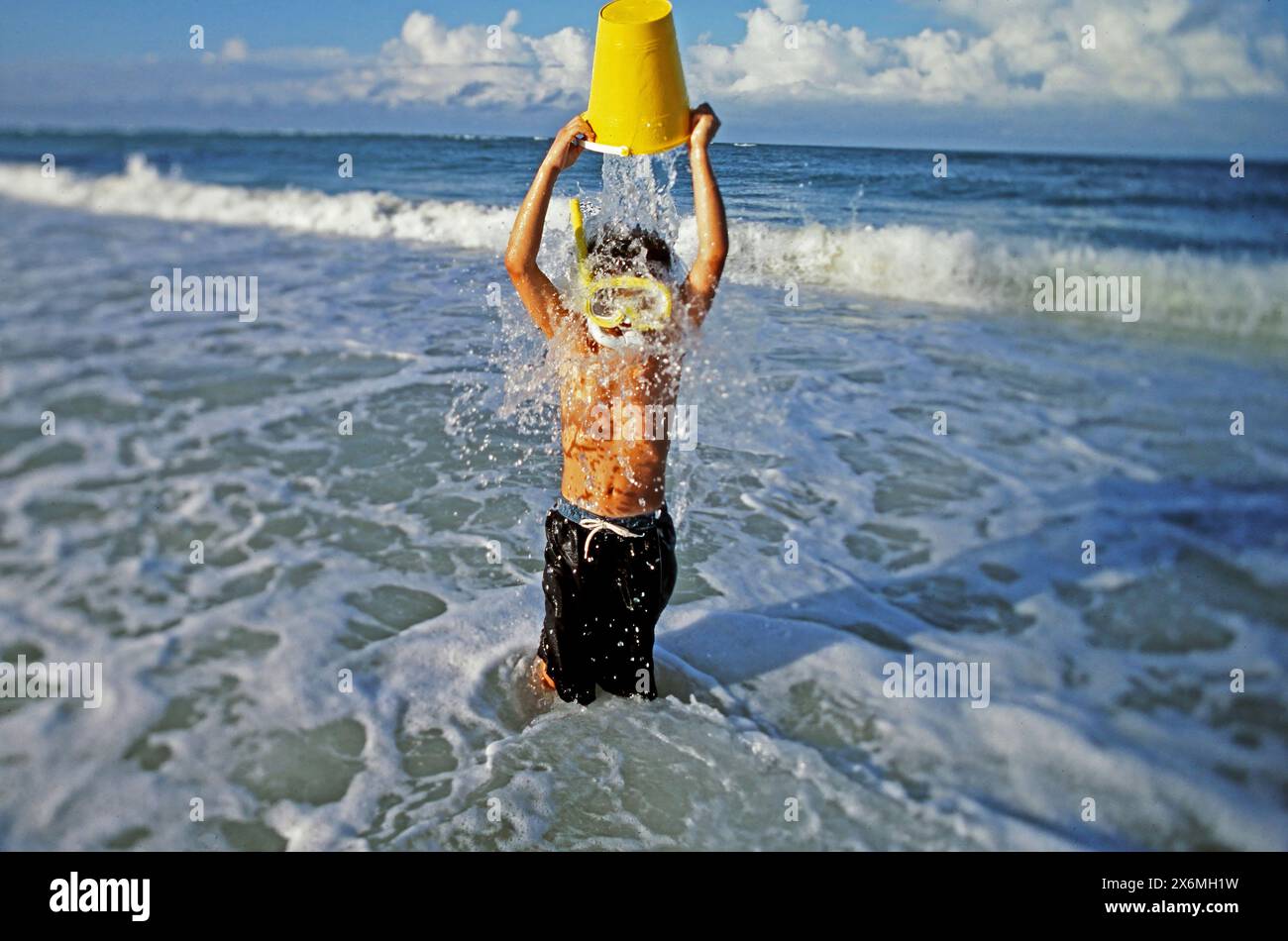 A young boy joyfully playing in the ocean water, holding a yellow ...