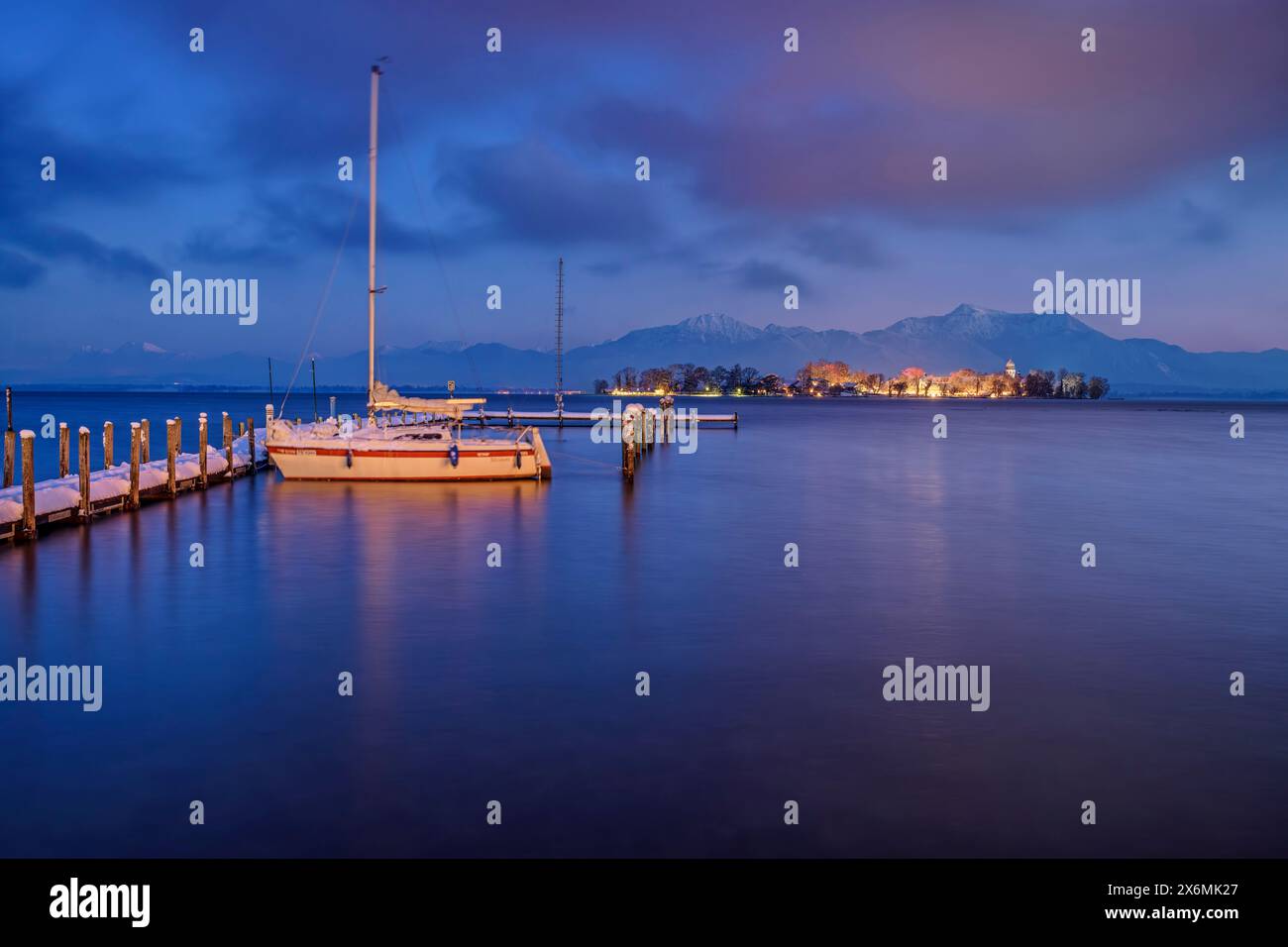 Snow-covered jetty with illuminated sailboat on Lake Chiemsee with ...