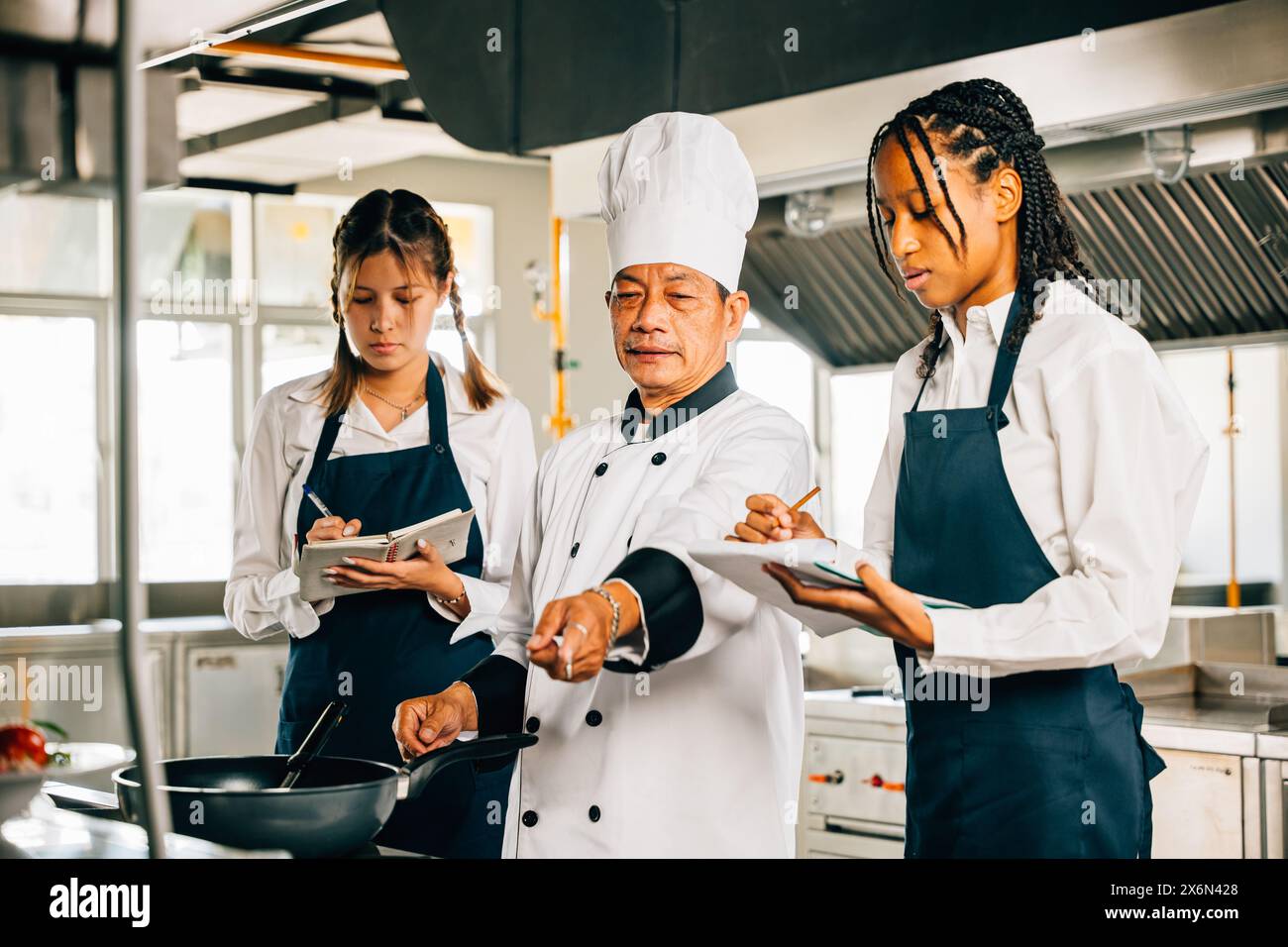 Asian senior chef in uniform teaches cooking techniques to multiracial ...