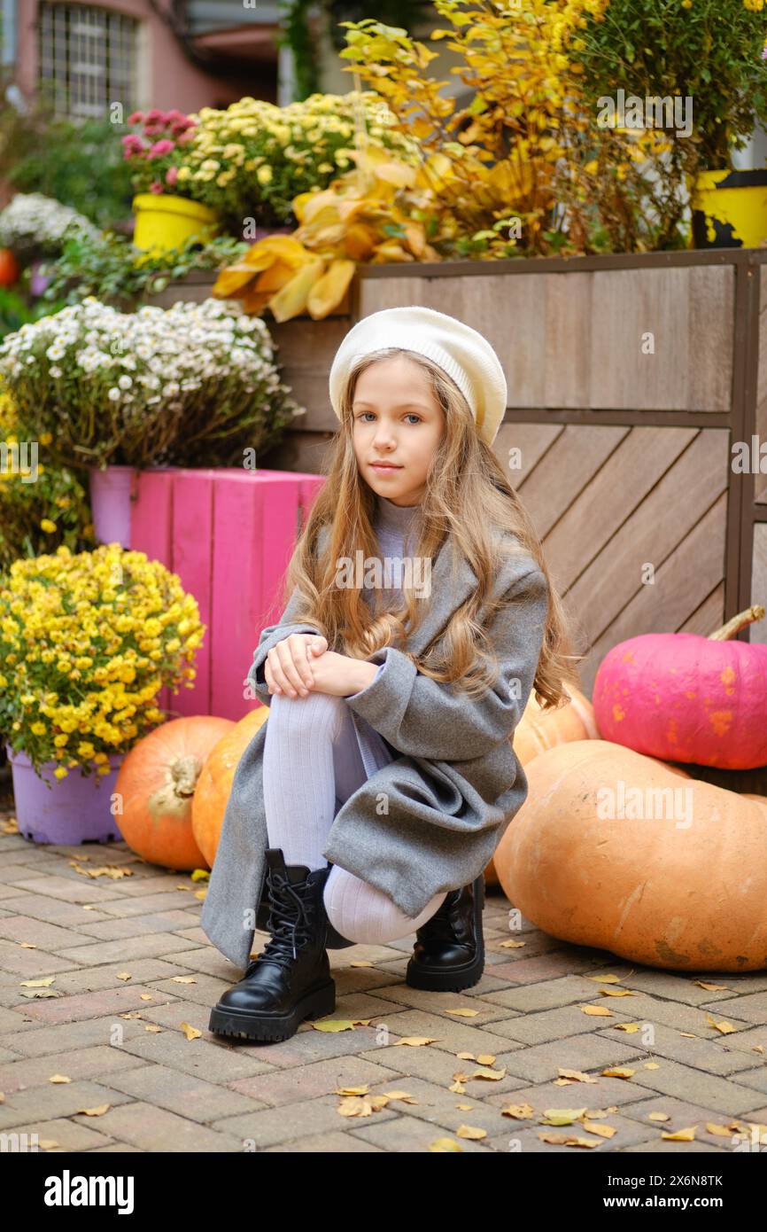 Little girl in a beret and wool coat sits on squats next to colorful ...
