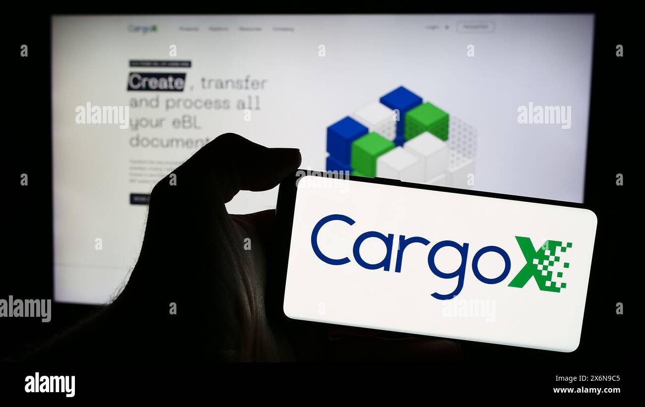 Person holding mobile phone with logo of Slovenian blockchain technology company CargoX Ltd. in ...