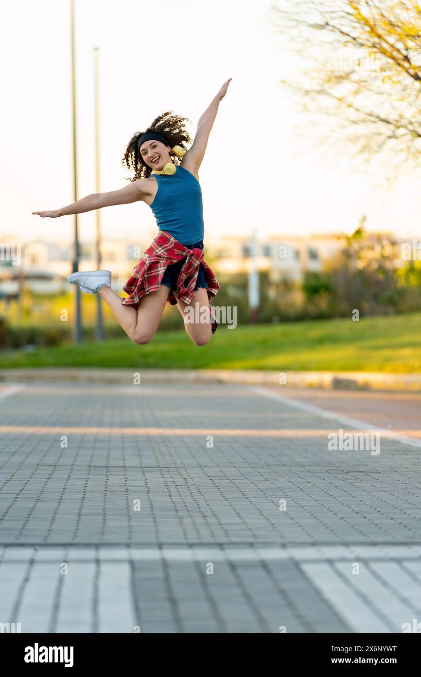Exhilarated young woman wearing headphones and a blue tank leaps ...