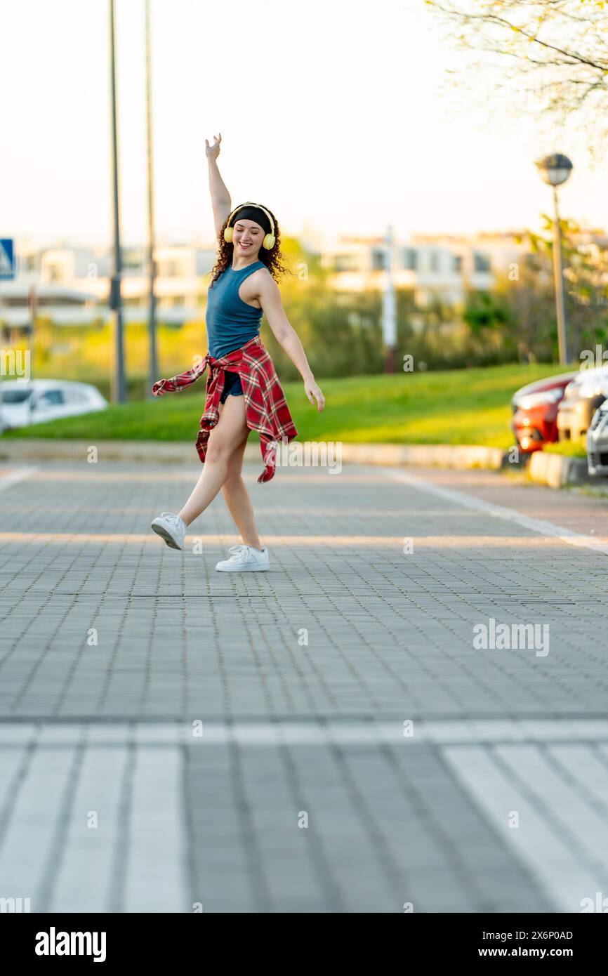 Vibrant young woman with curly hair dances joyfully on a city walkway ...