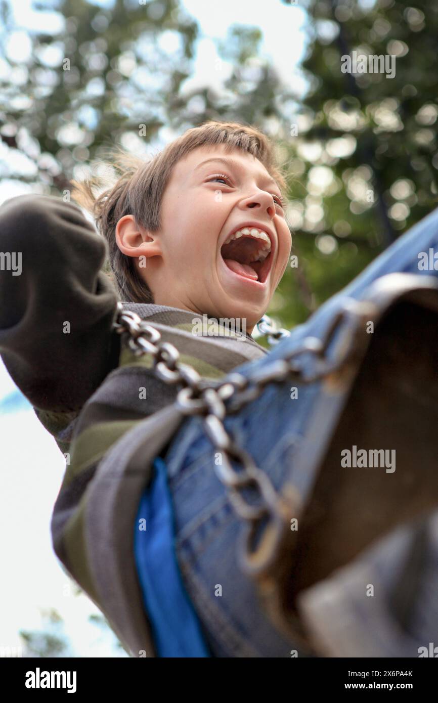 cheerful little boy on a swing on playground laughing Stock Photo - Alamy