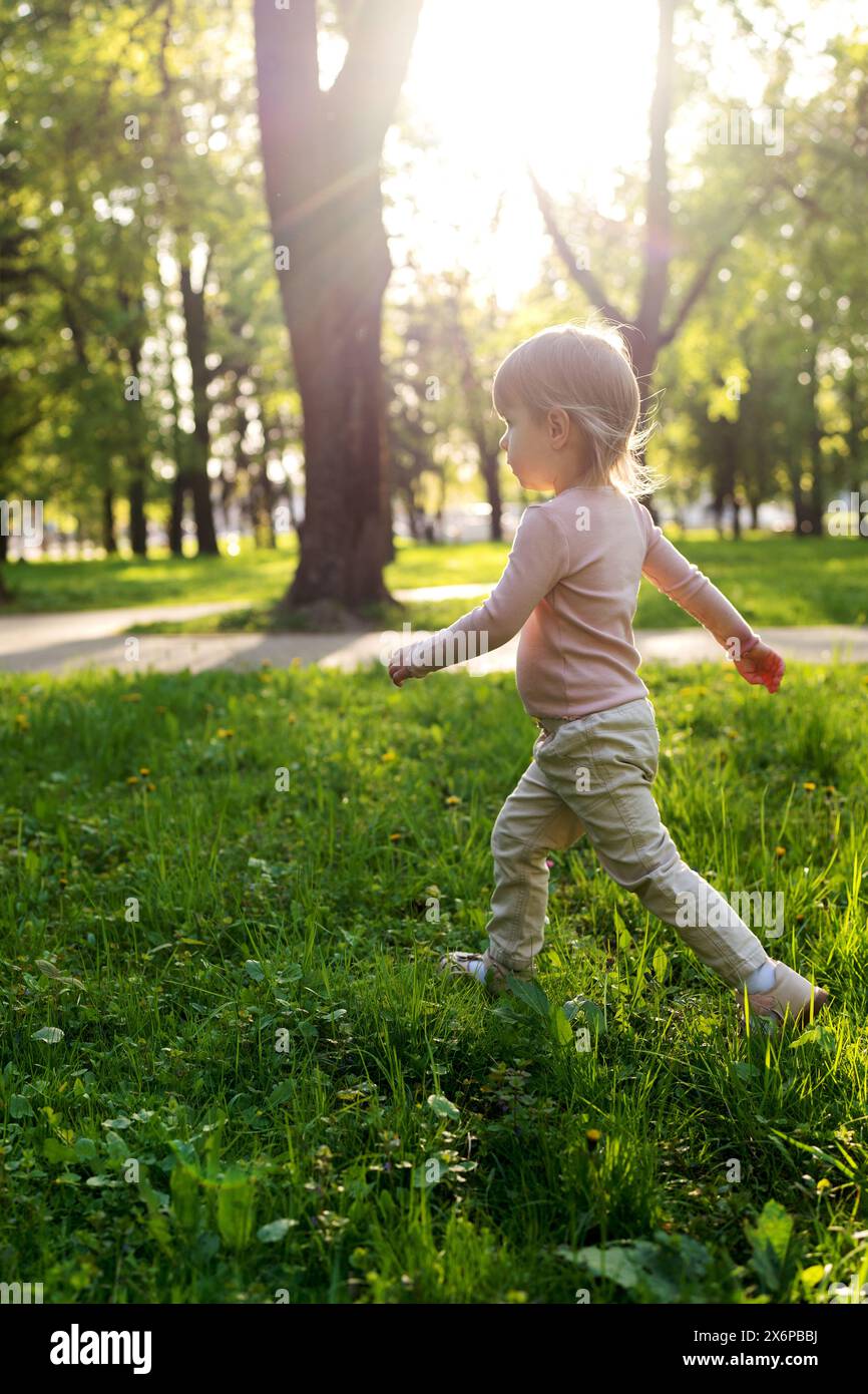 Happy child walking in the park at sunset. Green grass and leaves ...